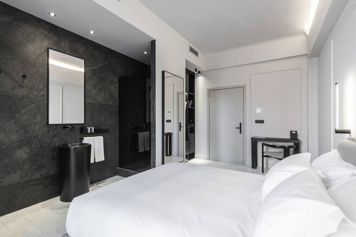 Quarto moderno com cama grande, toucador com espelho, lixeira preta e closet espaçoso.