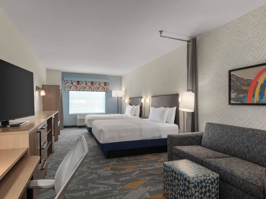 Quarto de hotel com cama, sofá, televisão e um quadro na parede.
