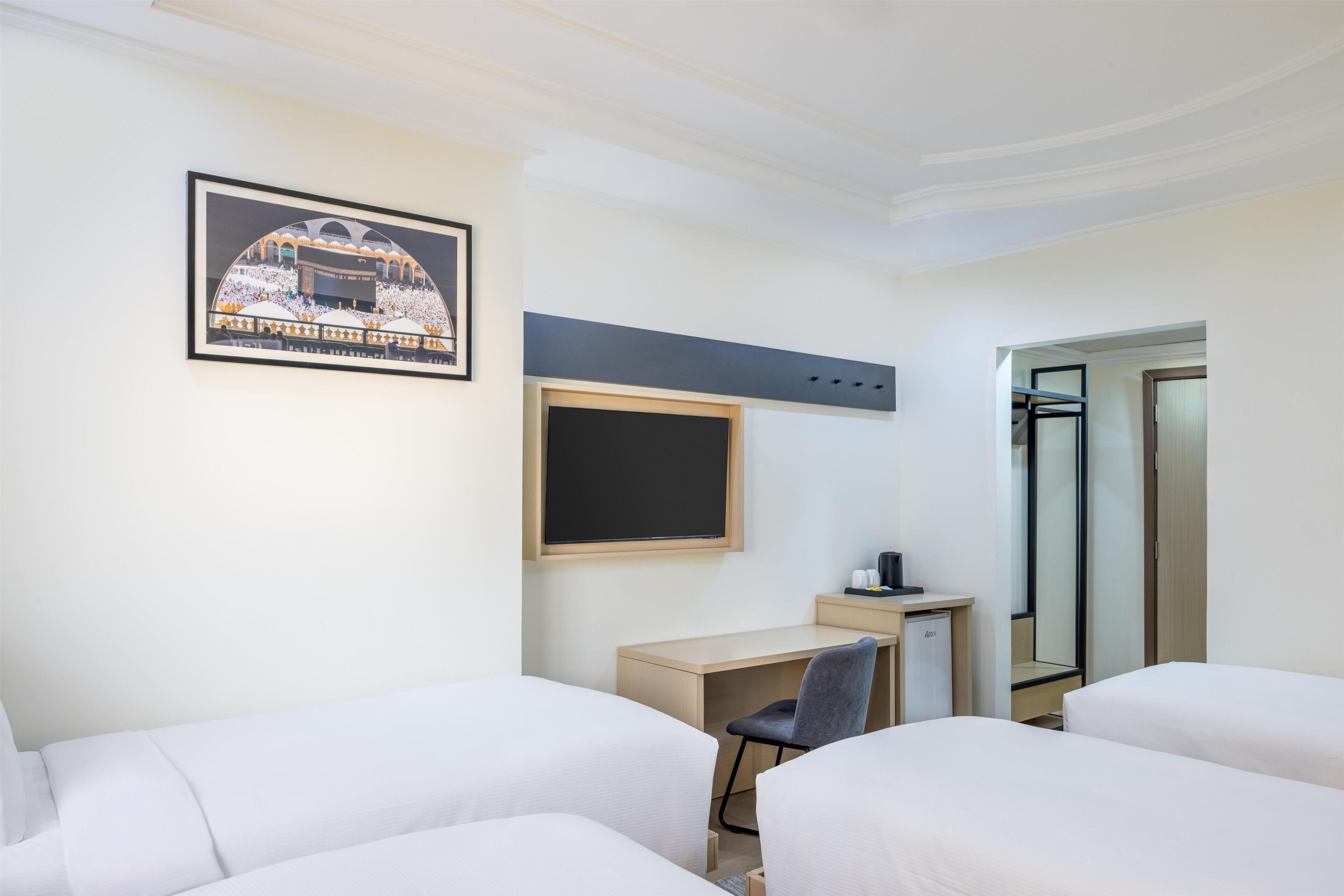 Quarto de hotel com duas camas, uma escrivaninha, uma cadeira, uma televisão, um espelho e um quadro na parede.