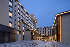 Um hotel moderno com um pátio central, vários andares e fachada bem iluminada.