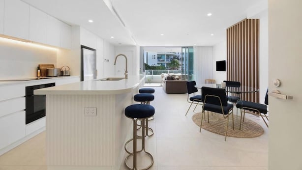 Uma cozinha moderna com uma ilha central, banquetas de bar e uma área de jantar com mesa redonda e cadeiras.