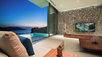 Sala de estar moderna com parede de pedra, uma janela ampla com vista para uma piscina e uma televisão de tela plana na parede.