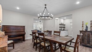 Uma sala de jantar com mesa e cadeiras de madeira, um lustre e um piano.