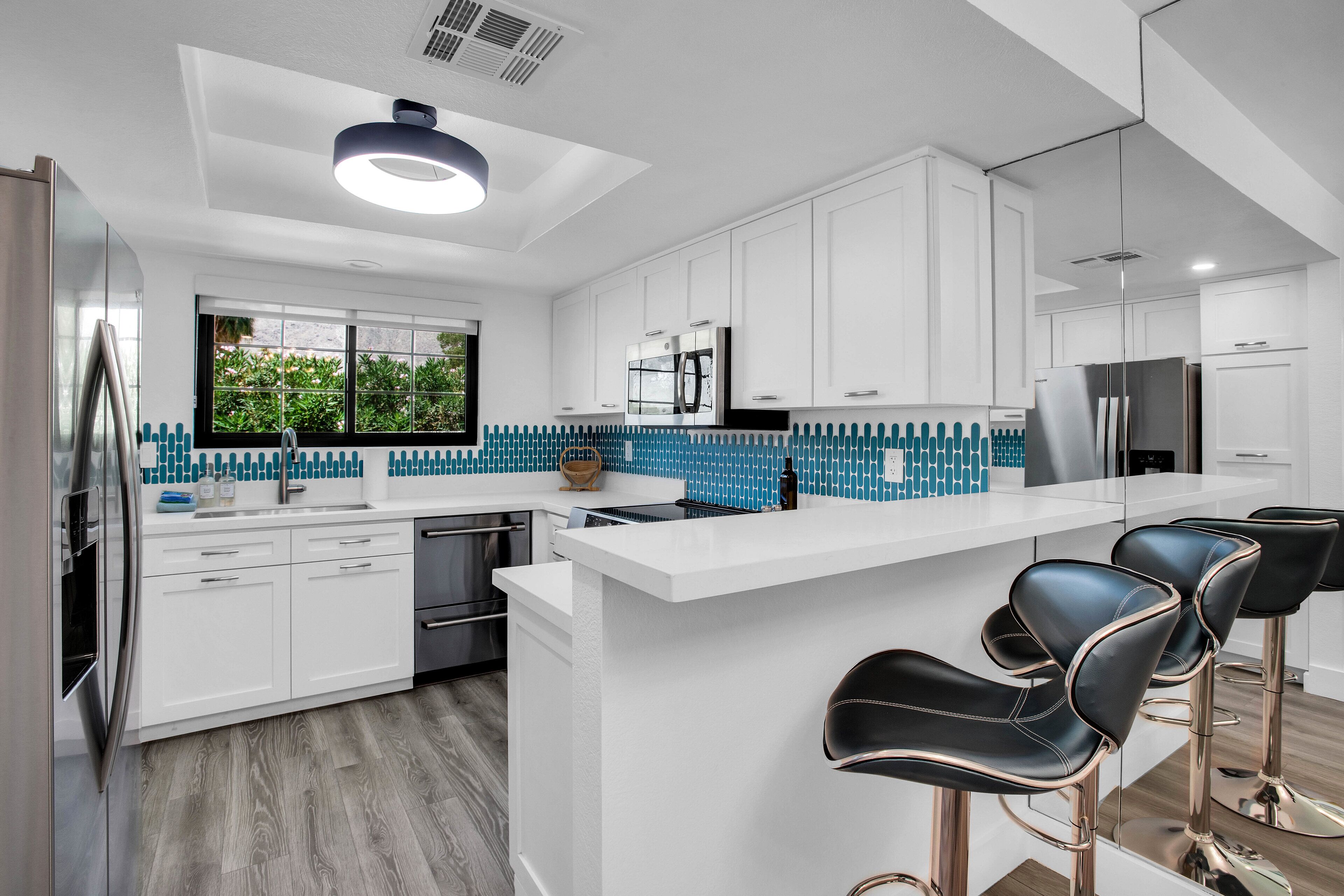 Uma cozinha moderna com armários brancos, uma ilha central com banquetas, eletrodomésticos de aço inoxidável e um revestimento azul.