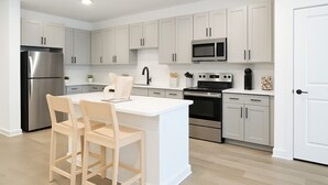 Cozinha moderna com armários brancos, eletrodomésticos de aço inoxidável e uma ilha central com cadeiras.