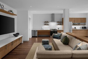Uma sala de estar moderna com televisão de tela plana, um sofá bege com almofadas, uma mesa de centro e armários de madeira.