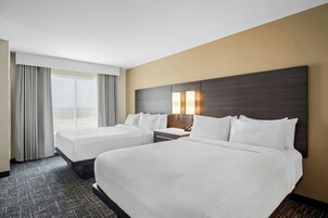 Quarto de hotel com duas camas, uma janela grande com cortinas e uma luminária na parede.