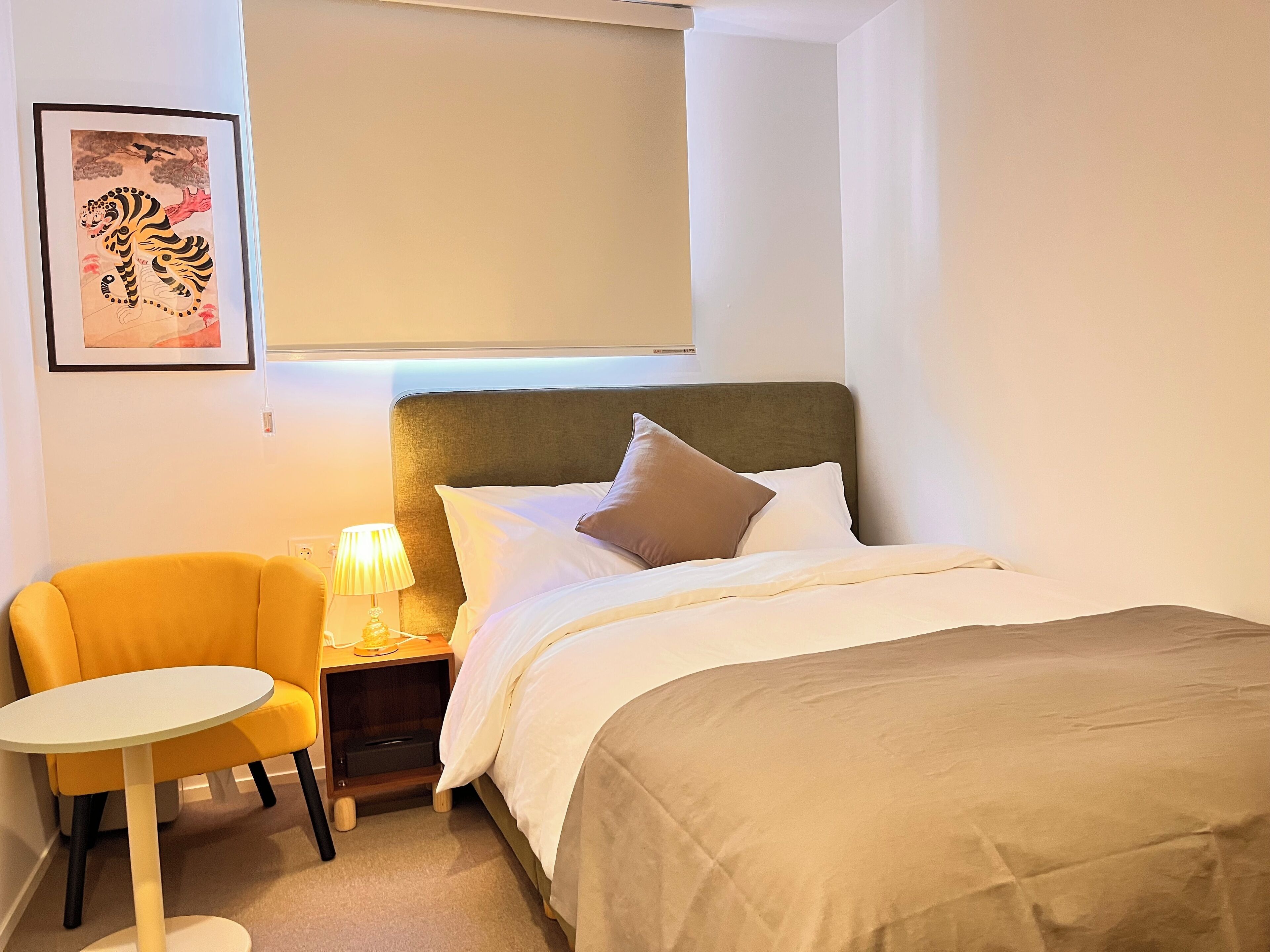 Quarto de hotel com uma cama, mesa de cabeceira, abajur, cadeira e quadro na parede.