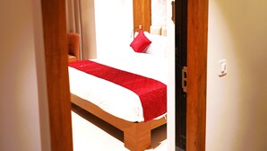 Quarto de hotel com cama, manta vermelha, cabeceira de madeira e ventilador de teto.