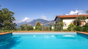 Piscina com vista para a montanha, rodeada por vegetação e um edifício com telhado de telhas vermelhas.