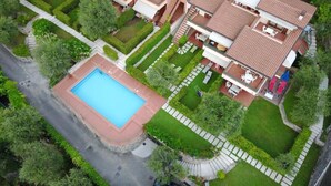 Vista aérea de uma propriedade residencial com piscina, vários edifícios e jardins bem cuidados.