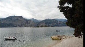 Um lago com barcos, uma margem rochosa e montanhas ao fundo.