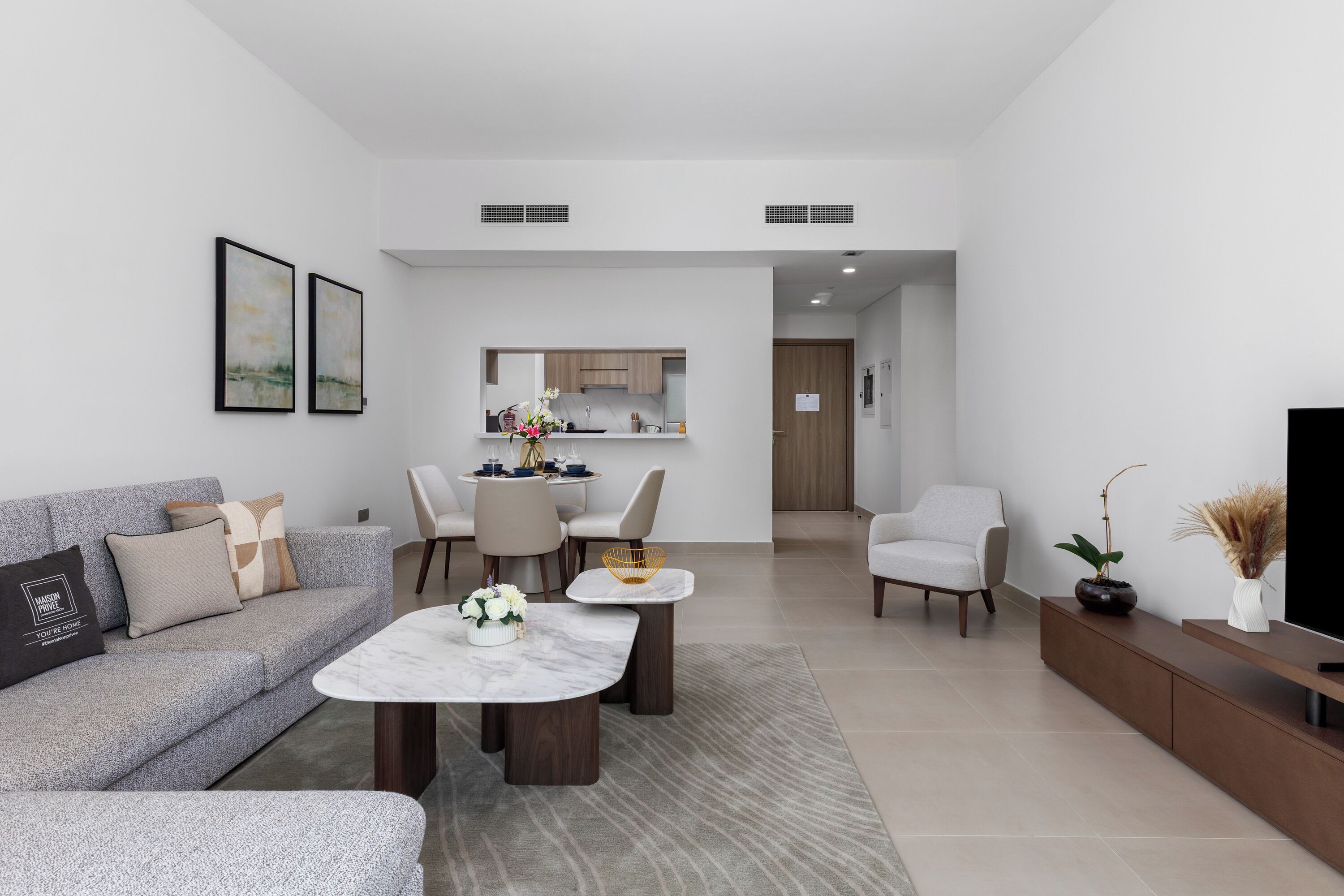 Uma sala de estar moderna com um sofá cinzento, uma mesa de centro e uma área de jantar com cadeiras e uma mesa.