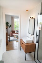 Casa de banho moderna com lavatório branco, espelho e chuveiro.