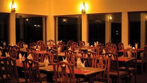 Restaurante com várias mesas e cadeiras, grandes janelas e luminárias fixadas na parede.