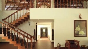 Uma escadaria que leva a um segundo andar, um corredor com uma porta no final e uma cadeira com um objeto decorativo ao lado.