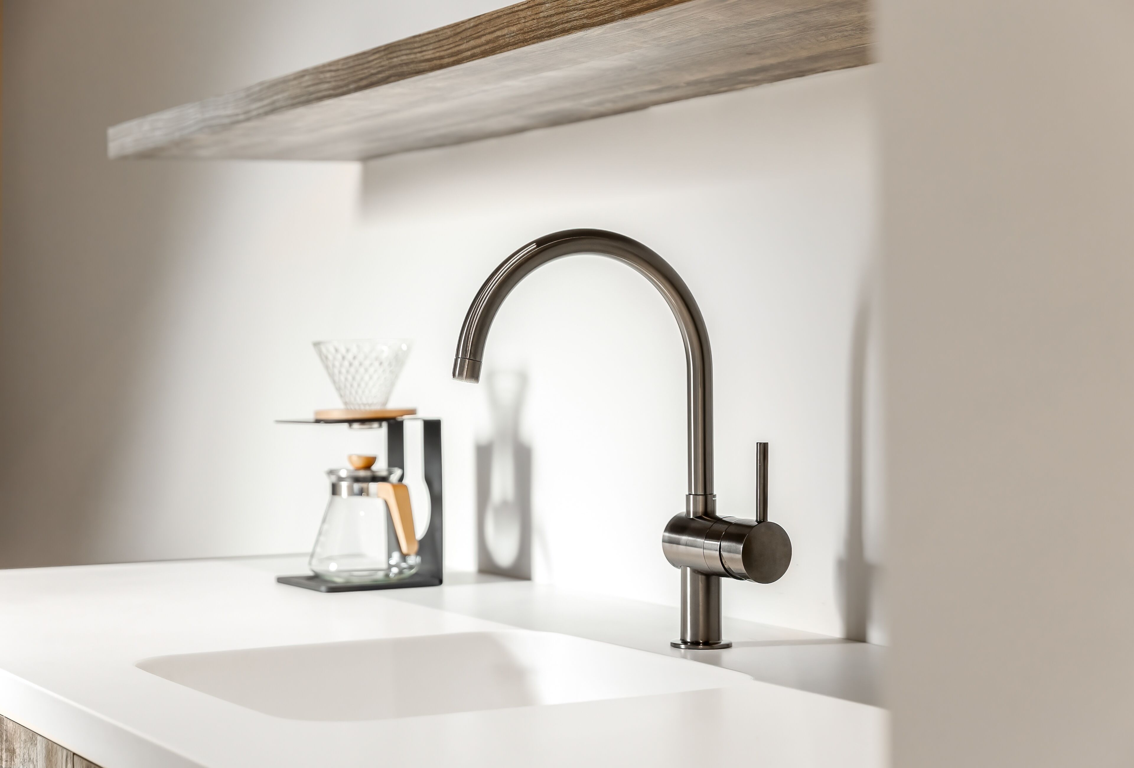 Uma cozinha moderna com uma torneira de aço inoxidável elegante, uma bancada branca e uma cafeteira.