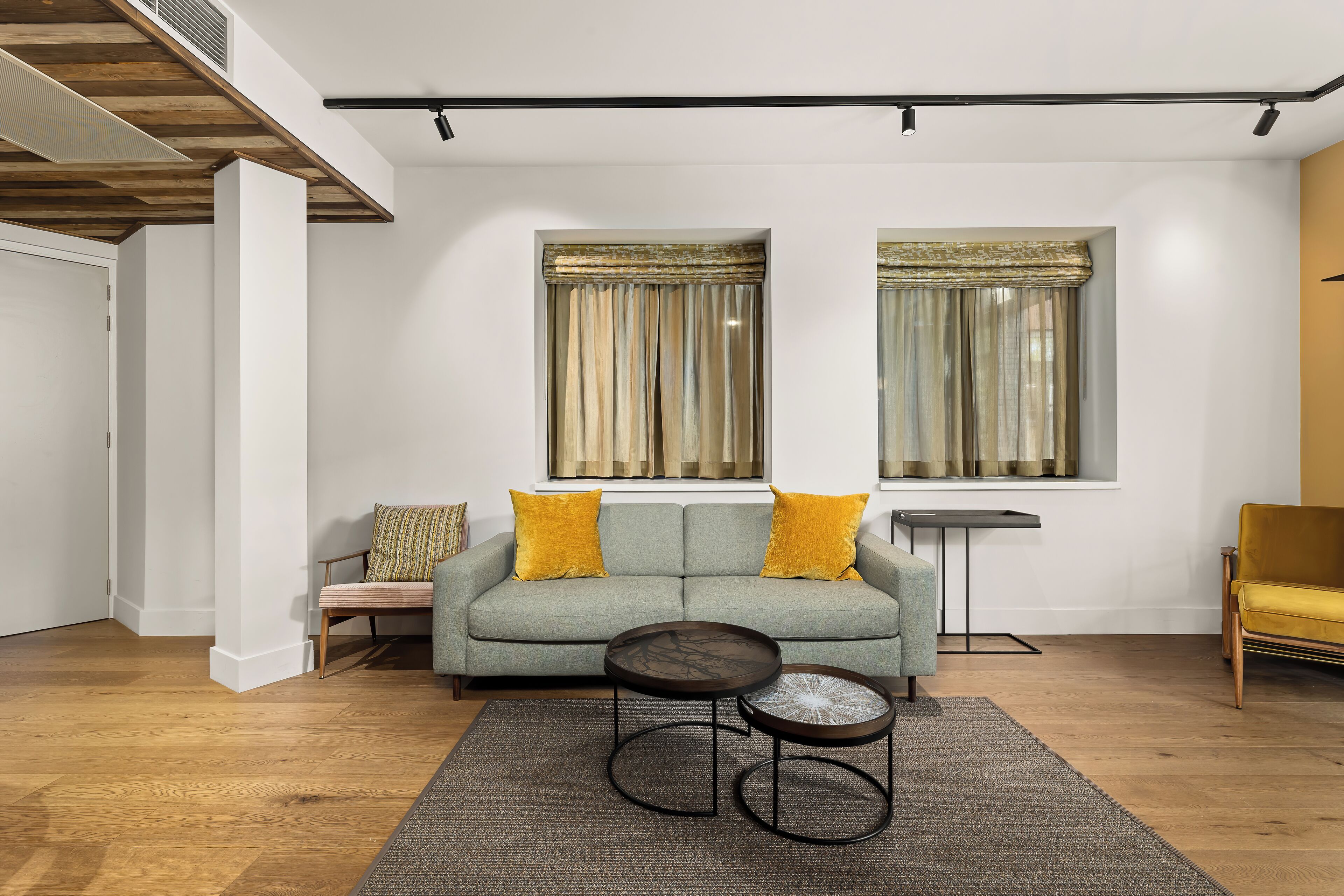 Uma sala de estar moderna com um sofá, duas mesas laterais e uma janela com cortinas.