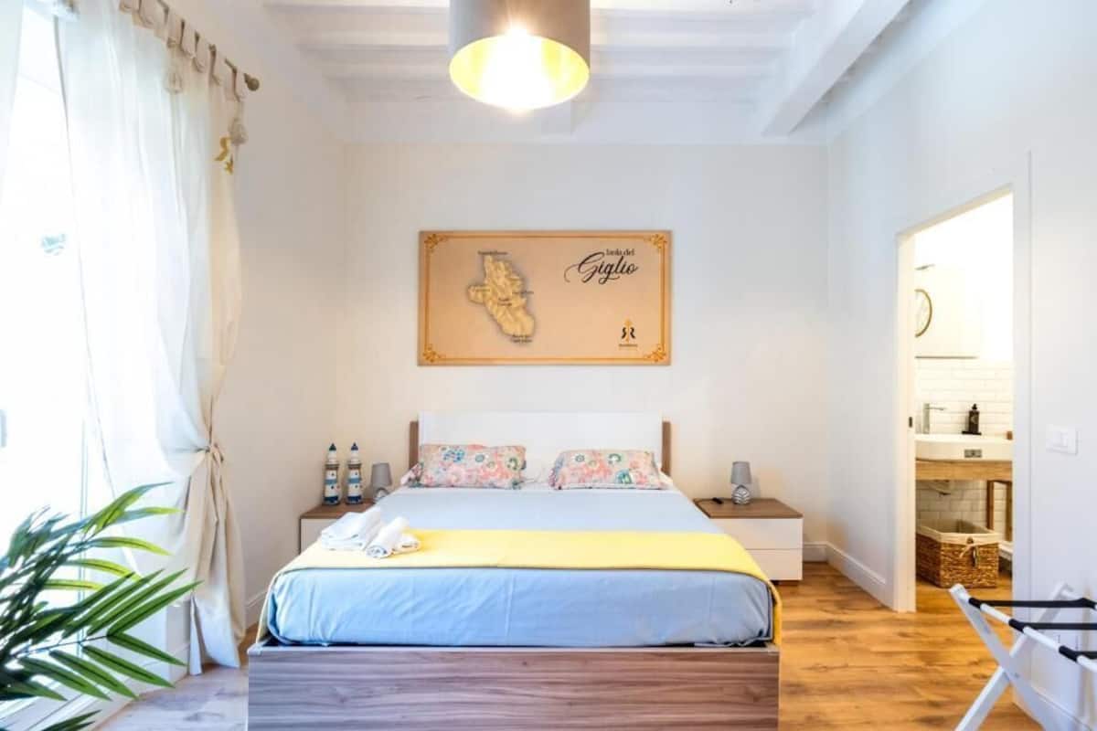 Quarto com cama, mesas de cabeceira, um mapa pendurado e uma janela com cortinas.