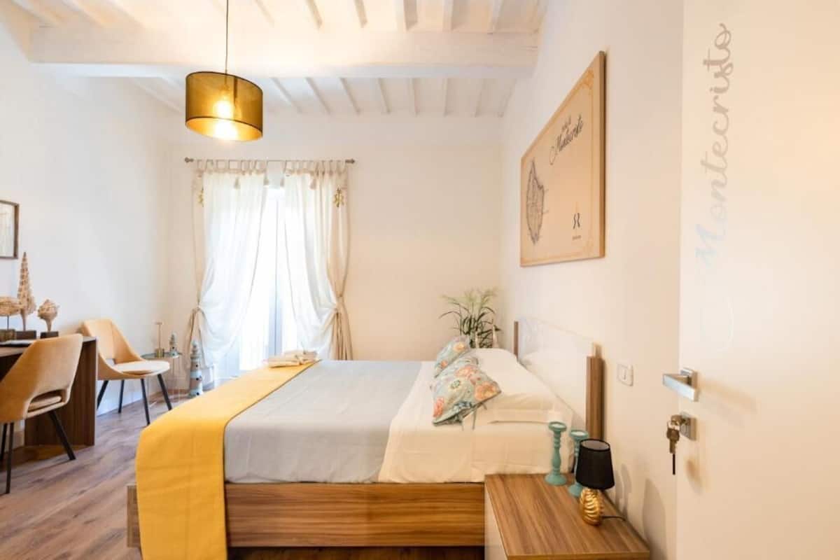 Quarto com cama, mesa de cabeceira, abajur e uma obra de arte na parede.