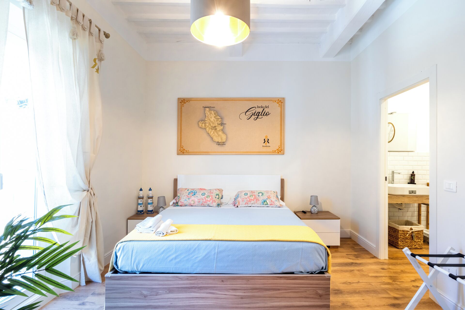 Quarto com cama, mesas de cabeceira, mapa na parede e vista para o banheiro.