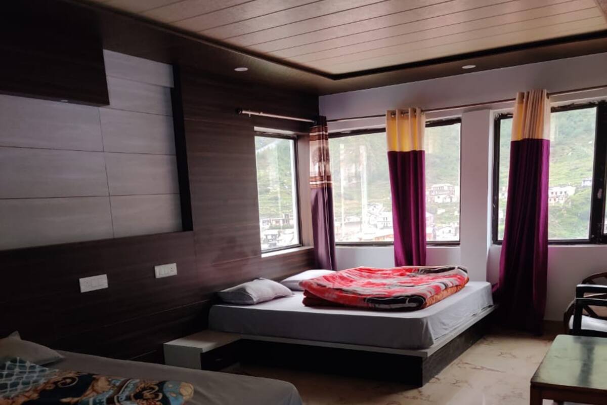 Quarto de hotel com cama, sofá-cama, mesa pequena e janela com cortinas.