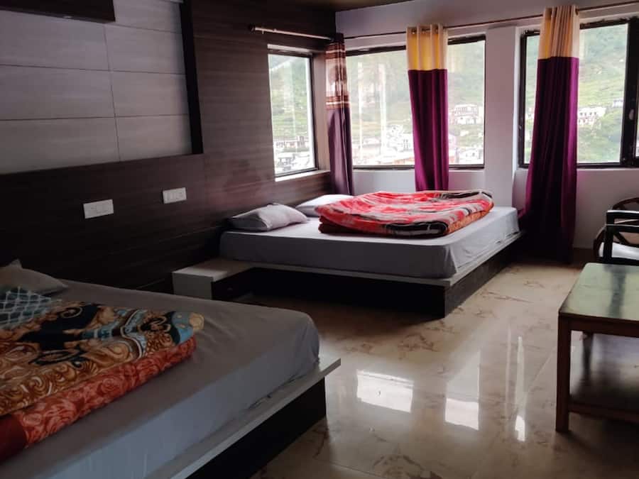 Quarto de hotel com cama, sofá-cama, mesa pequena e janela com cortinas.