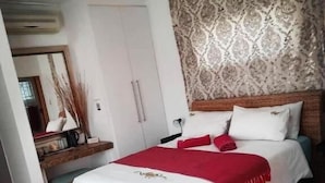 Um quarto com uma cama grande, cabeceira de madeira, mesa de cabeceira, um espelho e um papel de parede estampado.
