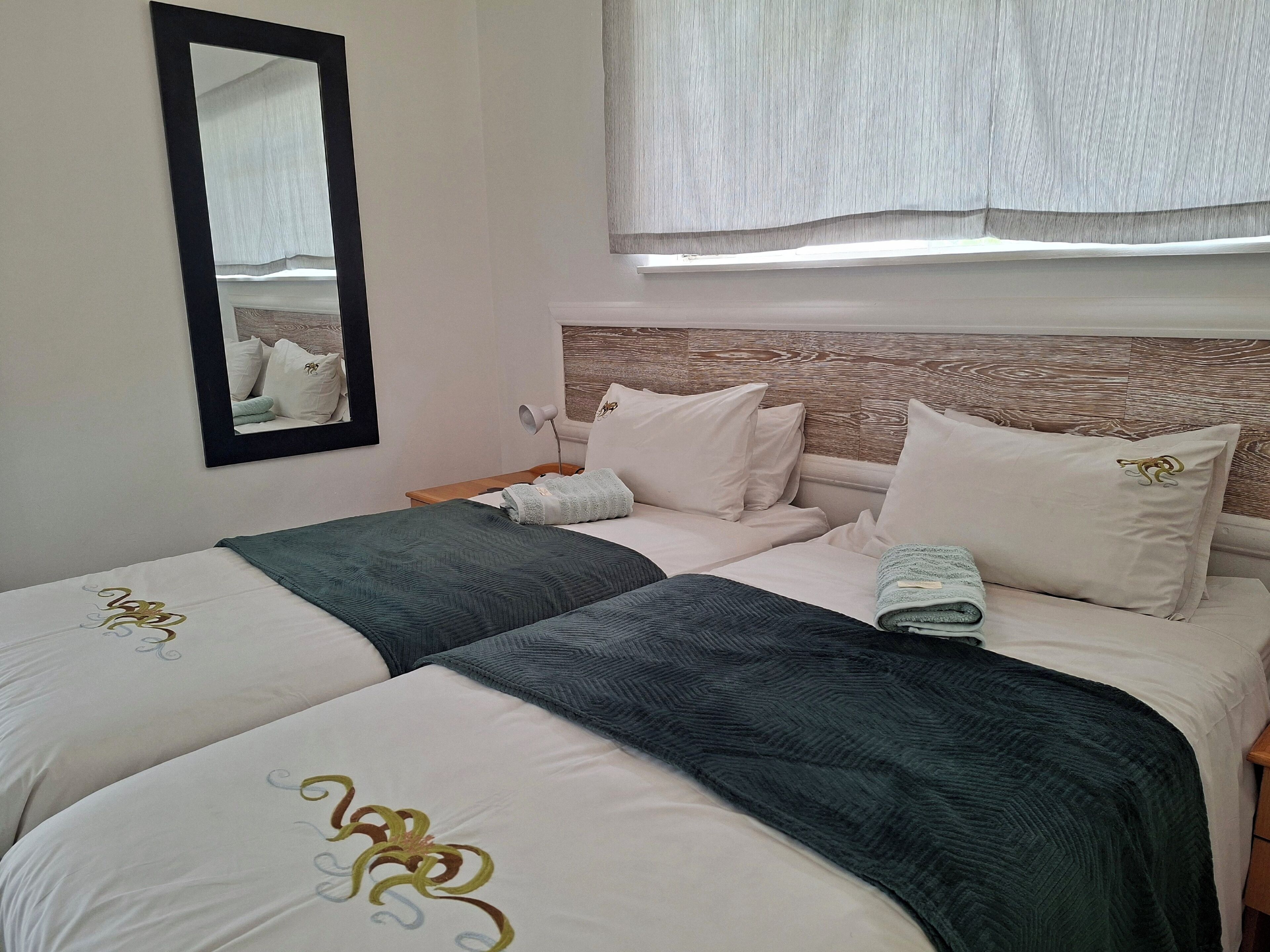 Quarto de hotel com duas camas, uma mesa de cabeceira, um espelho e uma janela com cortinas.
