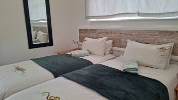 Quarto de hotel com duas camas, uma mesa de cabeceira, um espelho e uma janela com cortinas.
