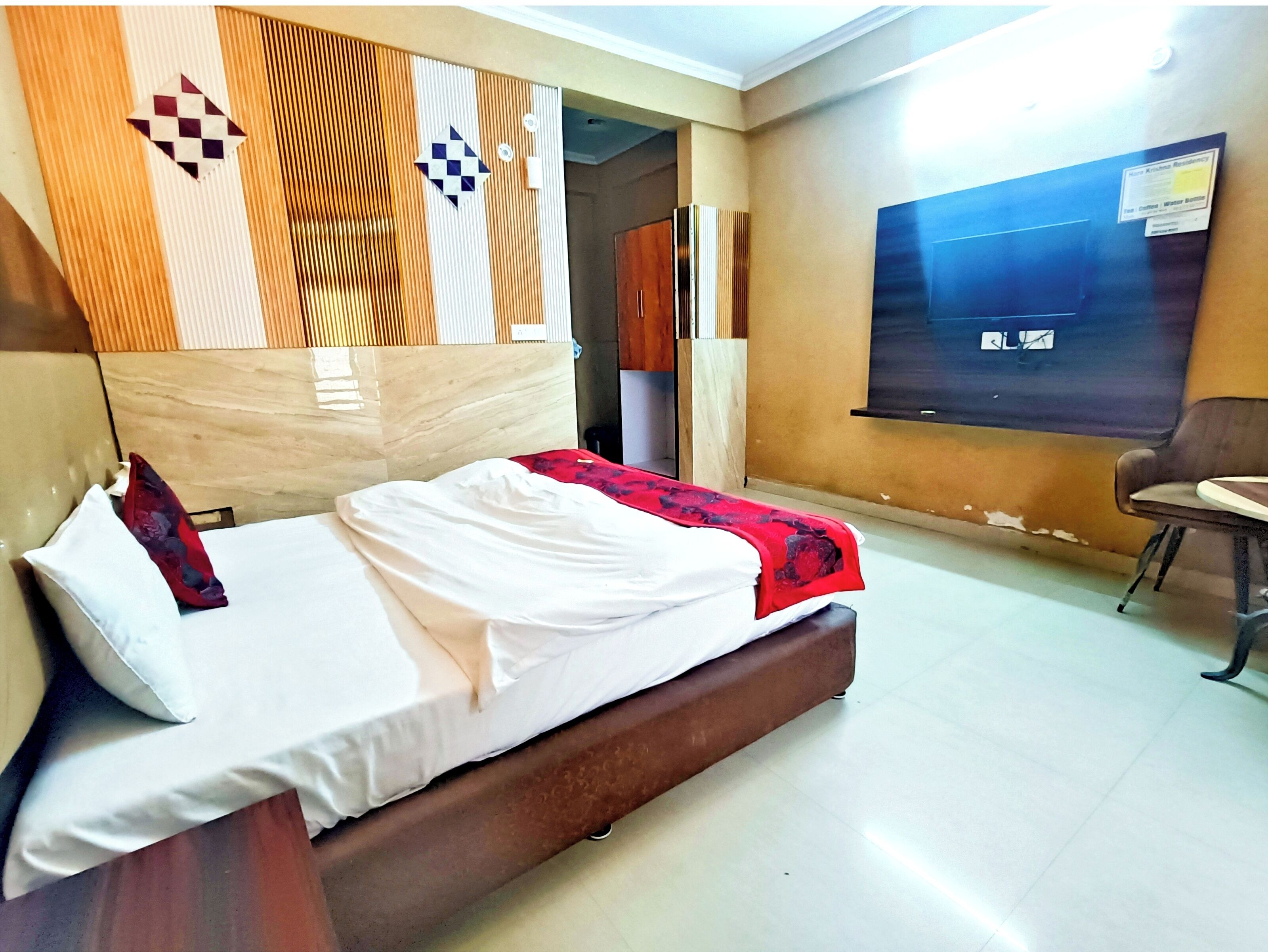 Quarto de hotel com uma cama, cabeceira de madeira, parede com padrão xadrez, televisão e uma cadeira.