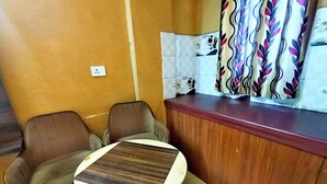 Um quarto pequeno com duas cadeiras de couro marrom, uma mesa redonda de madeira, um balcão de madeira e uma cortina estampada.