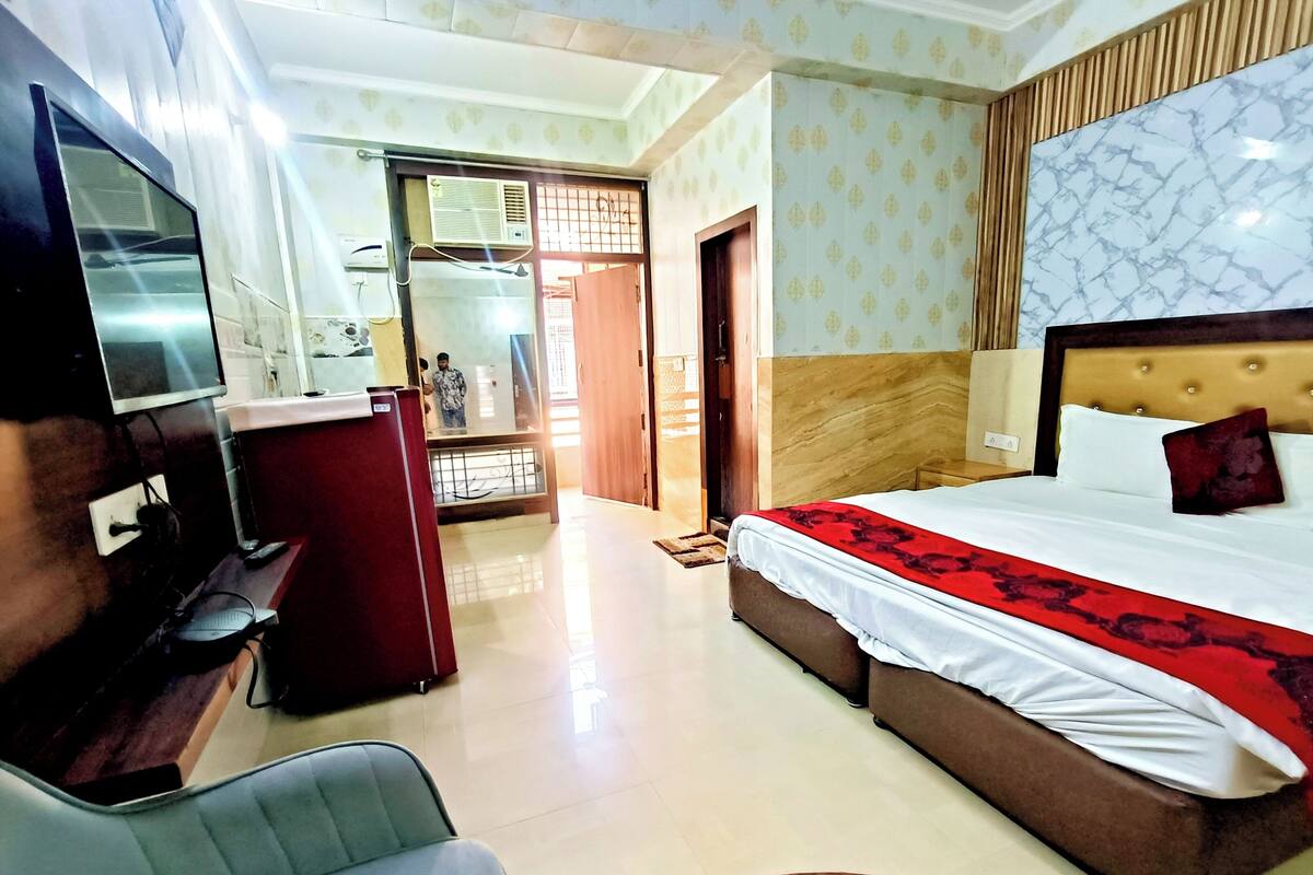 Quarto de hotel com uma cama, uma escrivaninha, uma televisão e um banheiro visível através de uma porta aberta.