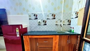 Cozinha com frigorífico, armários de madeira, bancada preta e azulejos estampados.