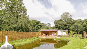 Uma cabana rústica com um lago, cercada por vegetação exuberante e árvores.