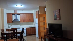 Uma cozinha compacta com armários de madeira, forno embutido, frigorífico e espaço de refeições com mesa e cadeiras.