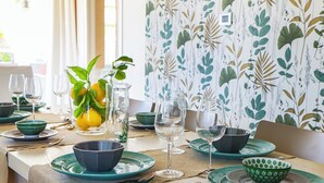 Uma mesa de jantar posta com pratos, tigelas e copos de vinho verdes, com um vaso de limões e uma planta verde sobre a mesa.