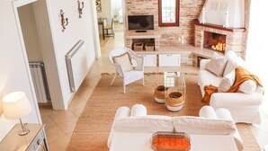 Sala de estar com lareira, sofás brancos, televisão e uma área de refeições ao fundo.