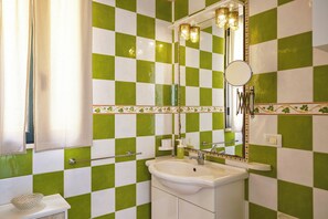 Um banheiro com azulejos quadriculados verdes e brancos, pia branca, espelho e porta-toalhas.