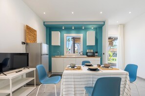 Uma cozinha moderna com uma parede de destaque azul-turquesa, uma área de jantar com cadeiras azuis e uma televisão sobre uma mesa branca.