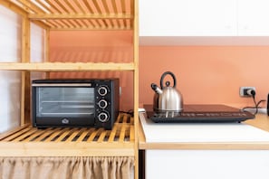 Uma cozinha compacta com forno tostador embutido e chaleira sobre uma bancada branca.