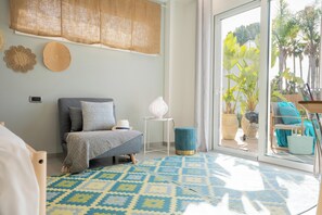 Quarto com cama, uma mesinha, abajur e vista para o exterior por uma porta de vidro deslizante.