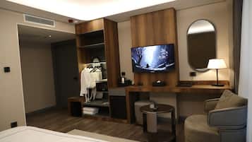 Quarto de hotel com cama, televisão, escrivaninha com luminária, cadeira, guarda-roupa e espelho.