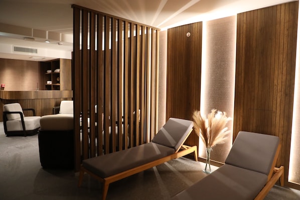 Uma área de estar moderna com duas poltronas confortáveis, uma divisória de madeira e uma pequena mesa decorada com plumas de capim-do-campo.