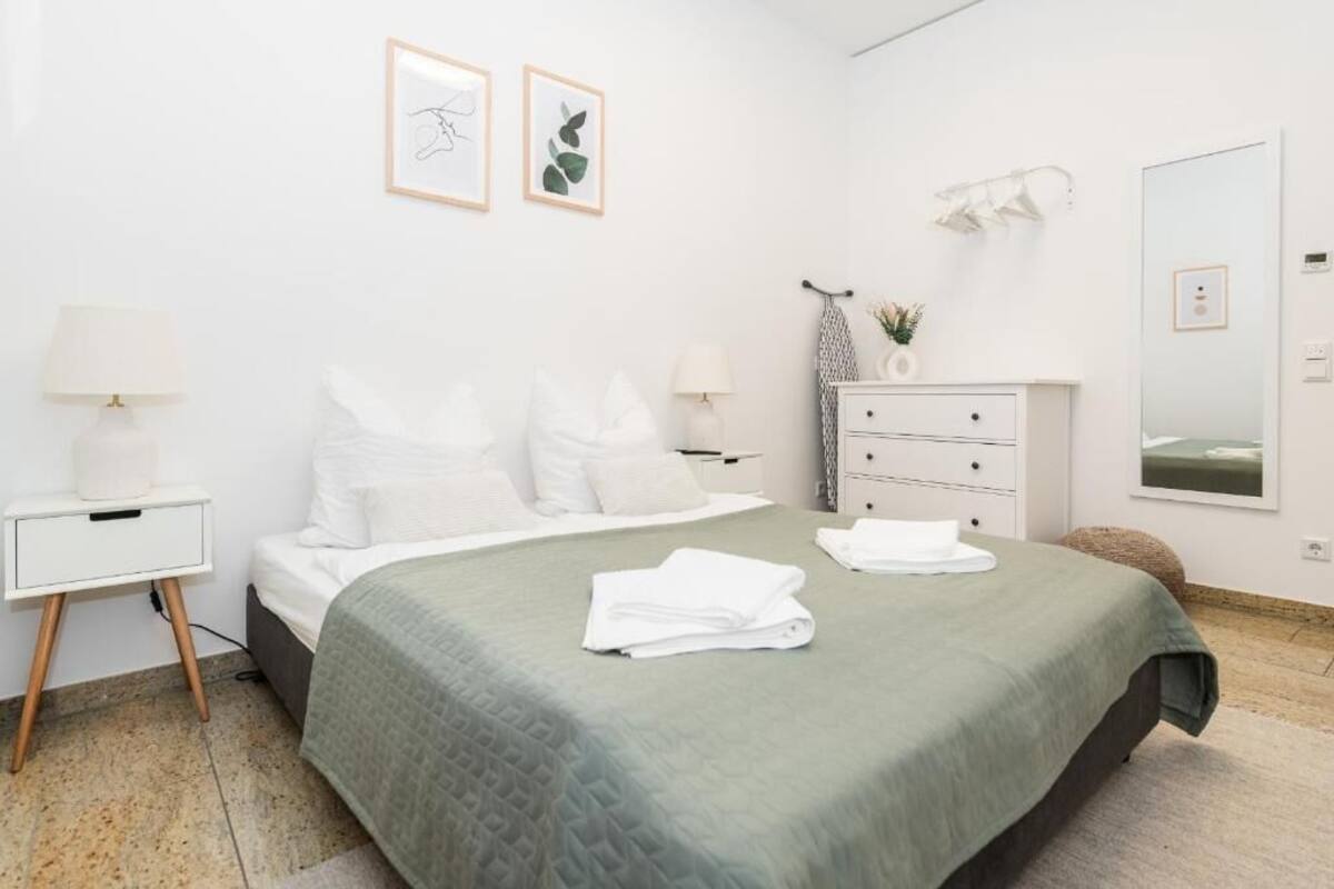 Quarto moderno com cama, mesas de cabeceira, cômoda e espelho.