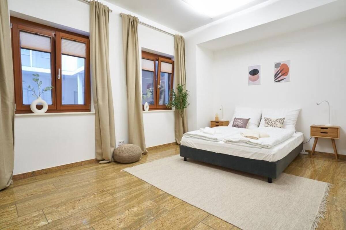 Quarto com cama, mesas de cabeceira, janela com cortinas, uma planta e obras de arte na parede.