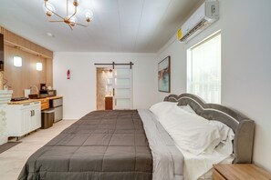 Quarto com uma cama grande, mesa de cabeceira, guarda-roupa, cozinha compacta e janela com persianas.
