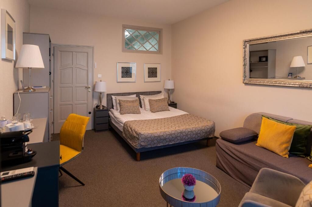 Quarto de hotel com cama, sofá, escrivaninha com luminária e espelho na parede.
