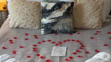 Uma cama bem arrumada com cabeceira estofada, roupa de cama branca e um travesseiro decorativo.