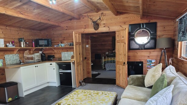 Interior acolhedor de uma cabana, com teto de madeira, cozinha compacta, sofá e cama.